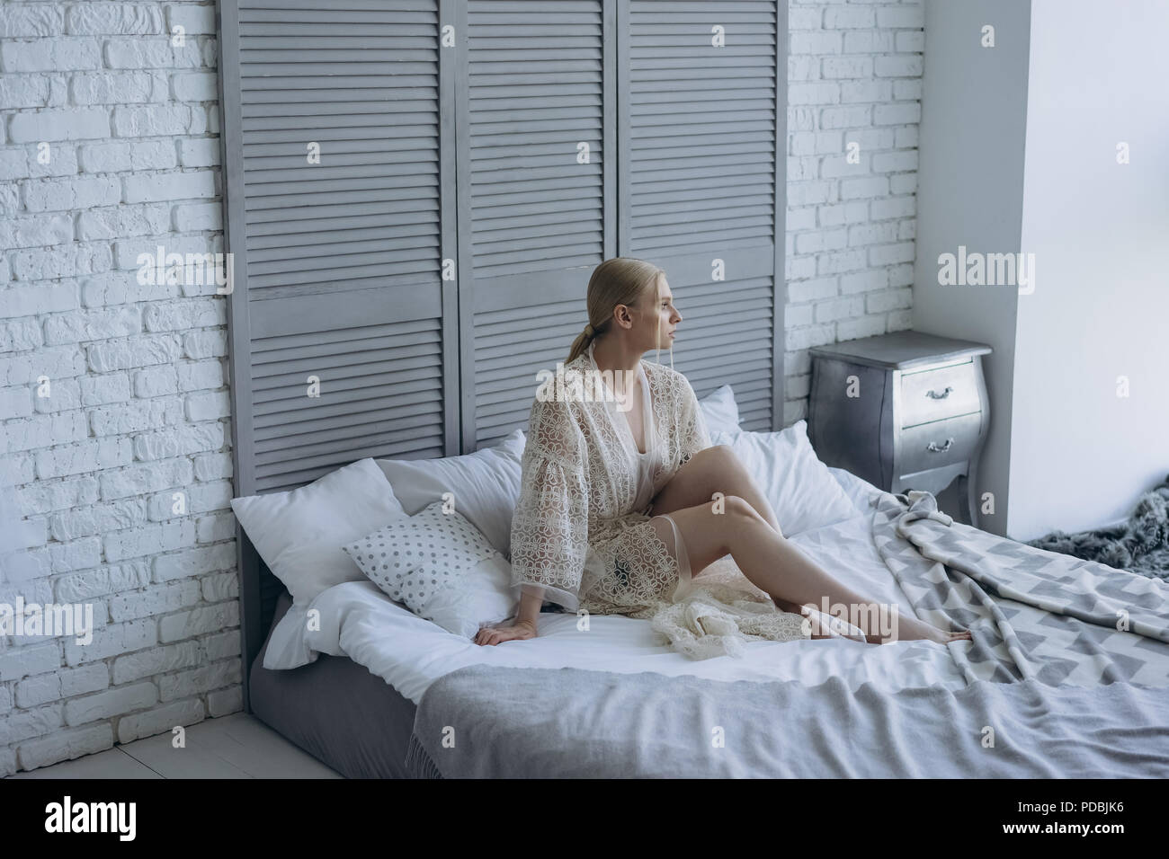 sensual young woman in negligee sitting on bed at morning and looking ...