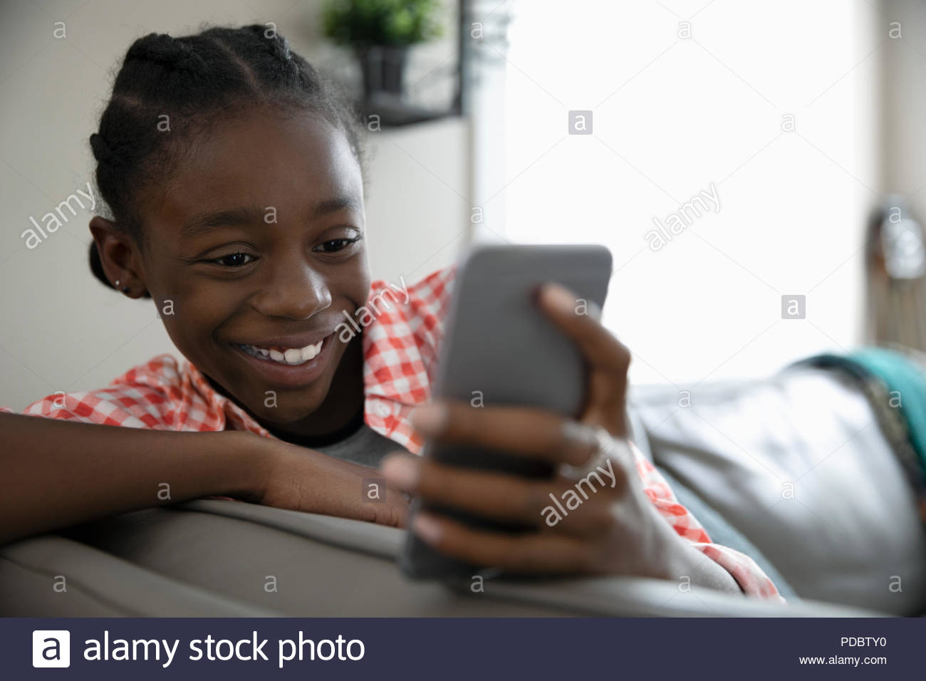 Smiling tween girl using smart phone on living room sofa Stock Photo ...