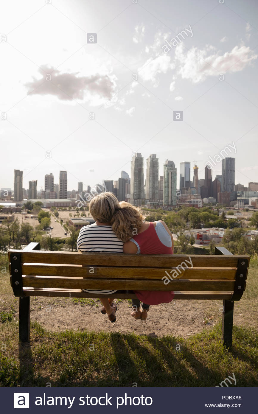 Affectionate mother and daughter on park bench overlooking sunny city ...