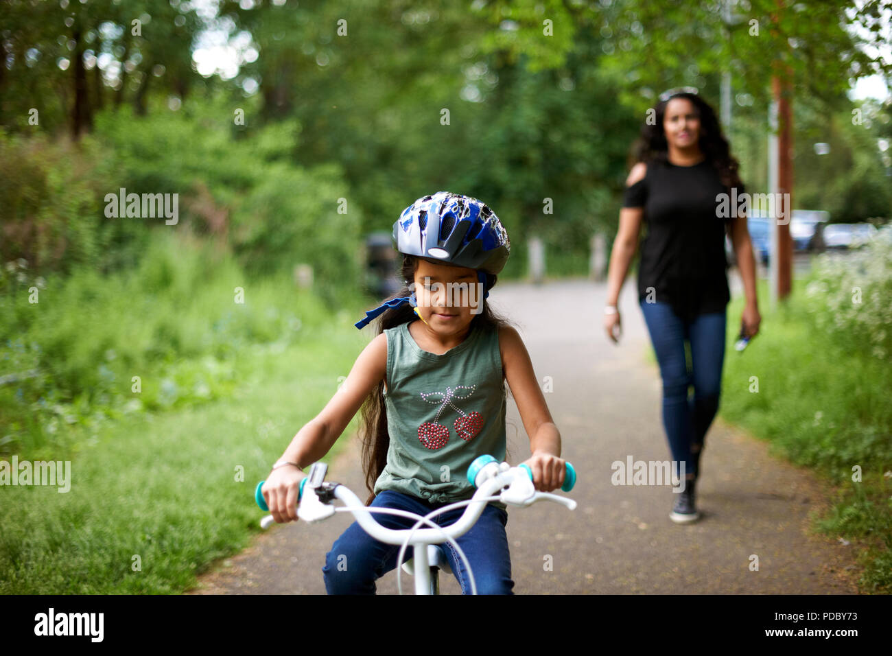 Mother watching daughter bike riding on path Stock Photo - Alamy