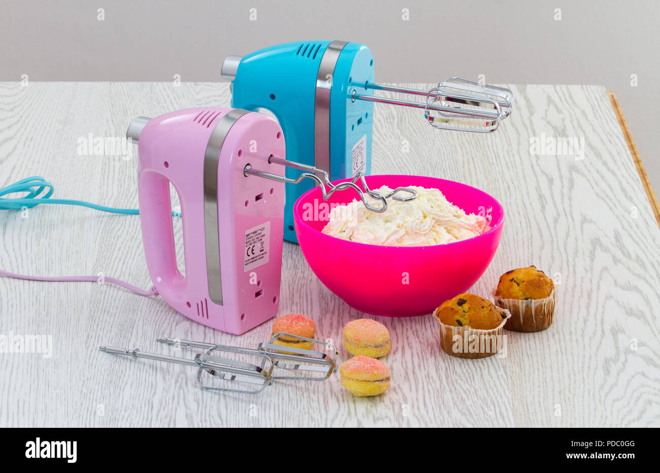 Colorful pink and blue kitchen mixers with whipped cream and cakes on ...