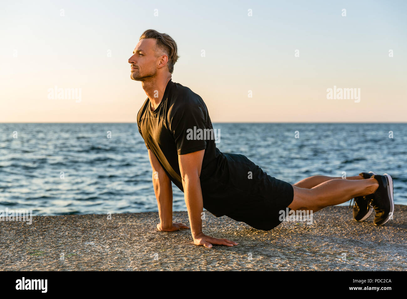 handsome adult sportsman doing backbend while stretching on seashore ...