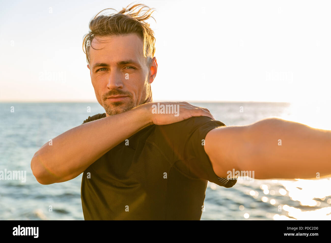 athletic adult man stretching arm before training on seashore Stock ...