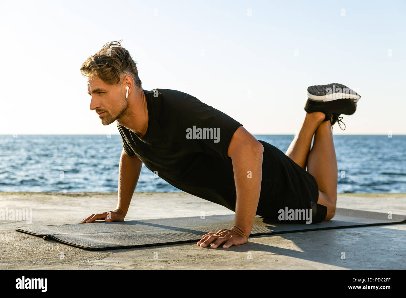 sporty adult man with wireless earphones doing push ups on knees on ...