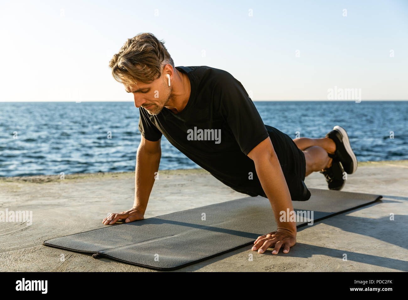 adult sportsman with wireless earphones doing push ups on seashore ...