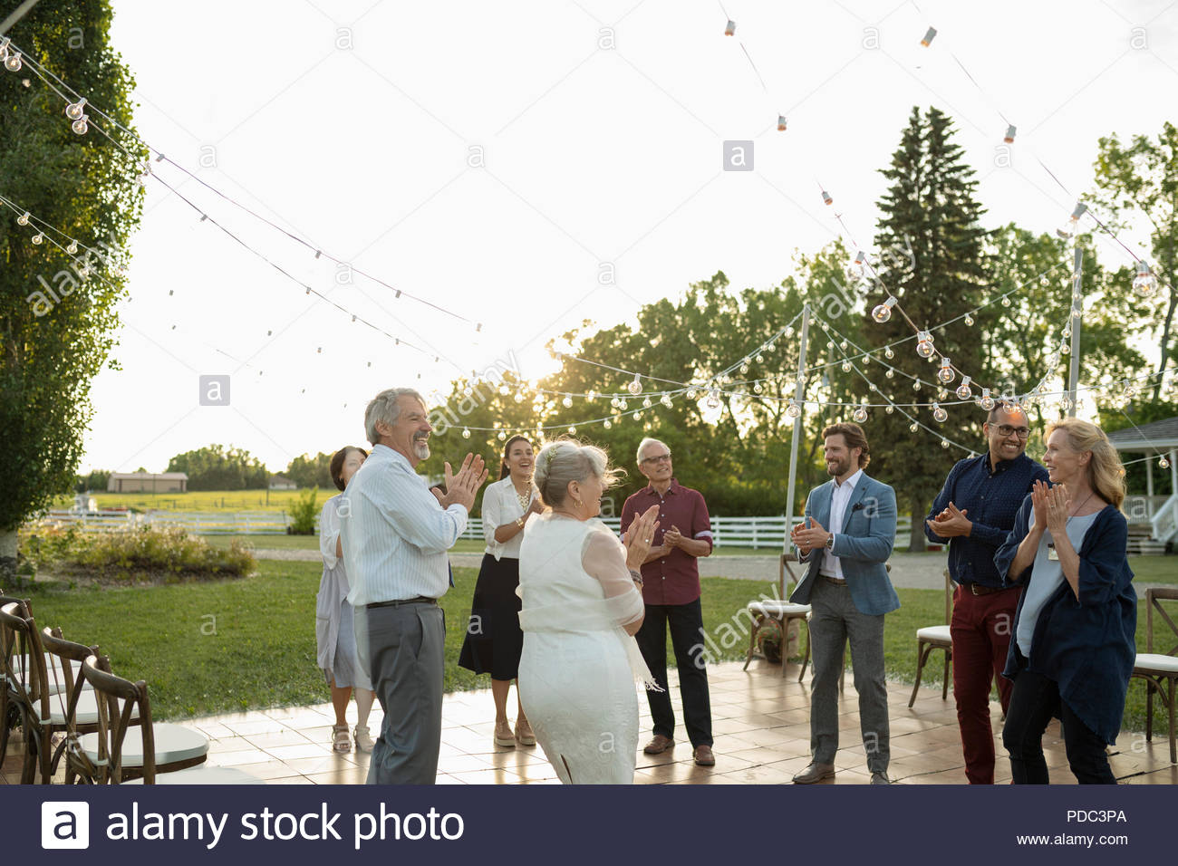 Friends and senior bride and groom clapping at wedding reception in ...