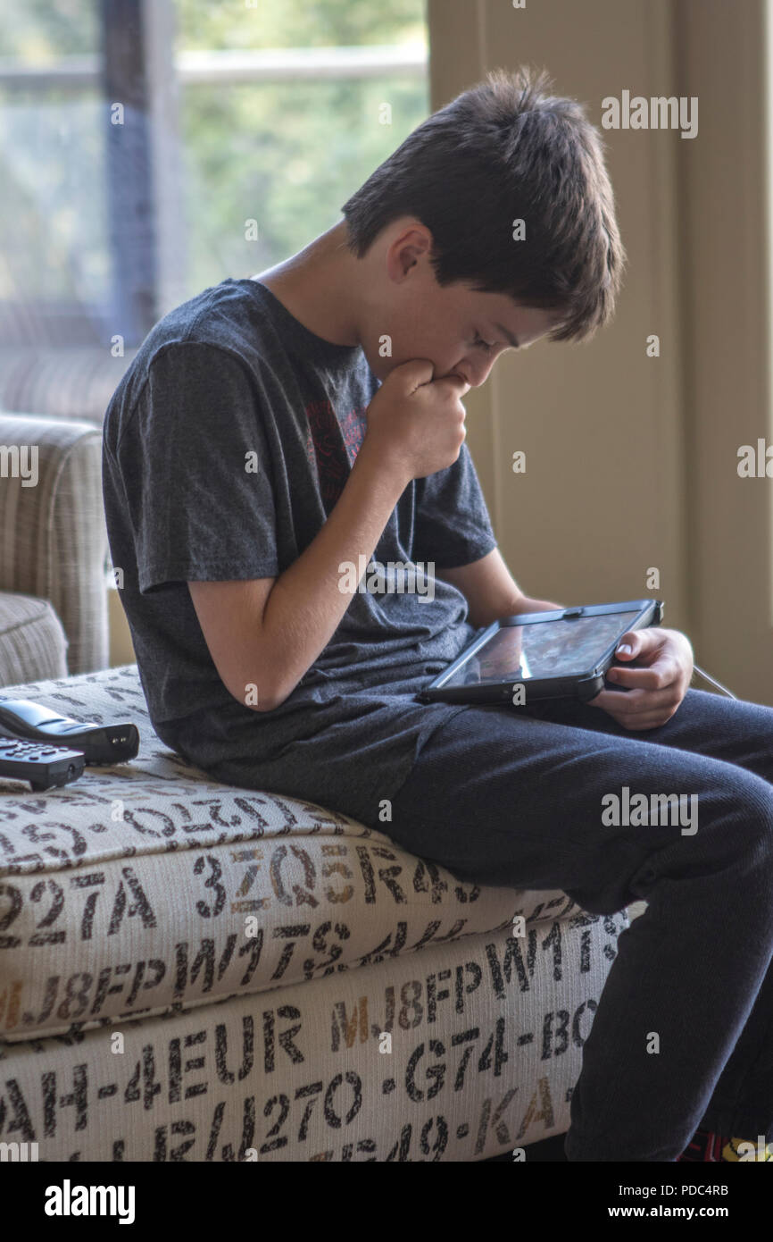 Cute male child playing on iPad, side veiw, looking down, vertical and ...