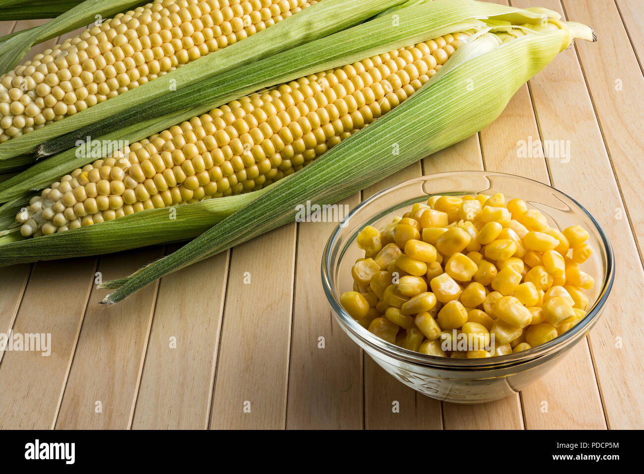 Fresh corn on the cob with leaves and grains on wooden table Stock ...
