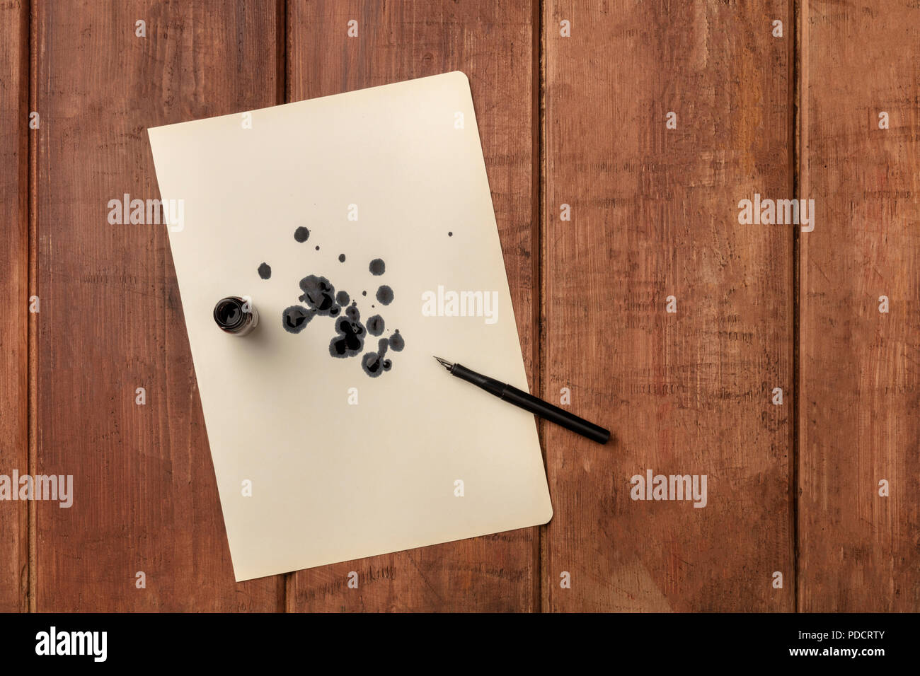 An overhead photo of an ink well with drops of ink on paper, with a nib ...