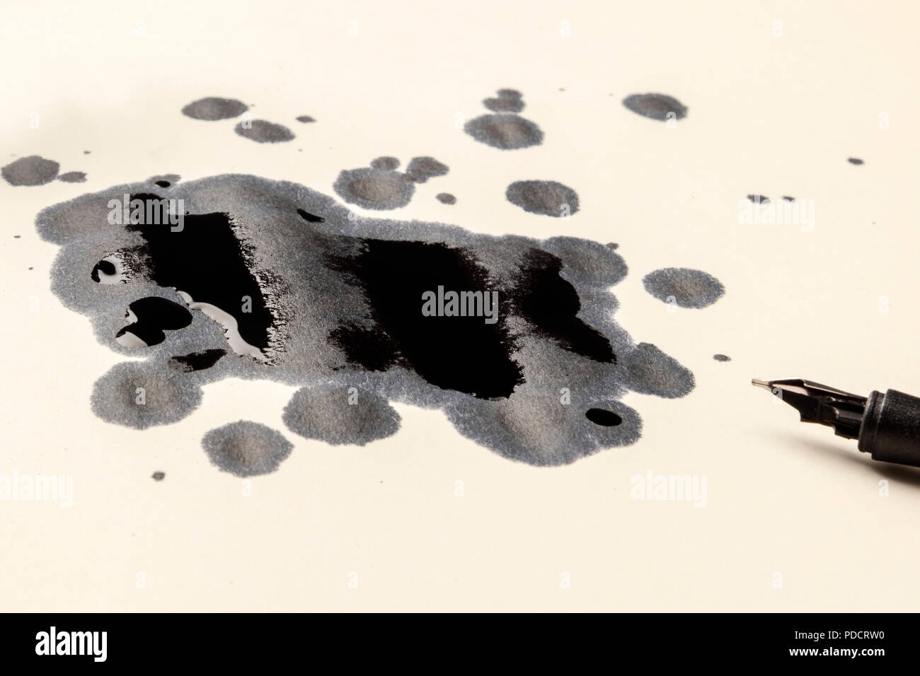 A photo of drops of ink on a textured off-white paper, with a nib pen ...