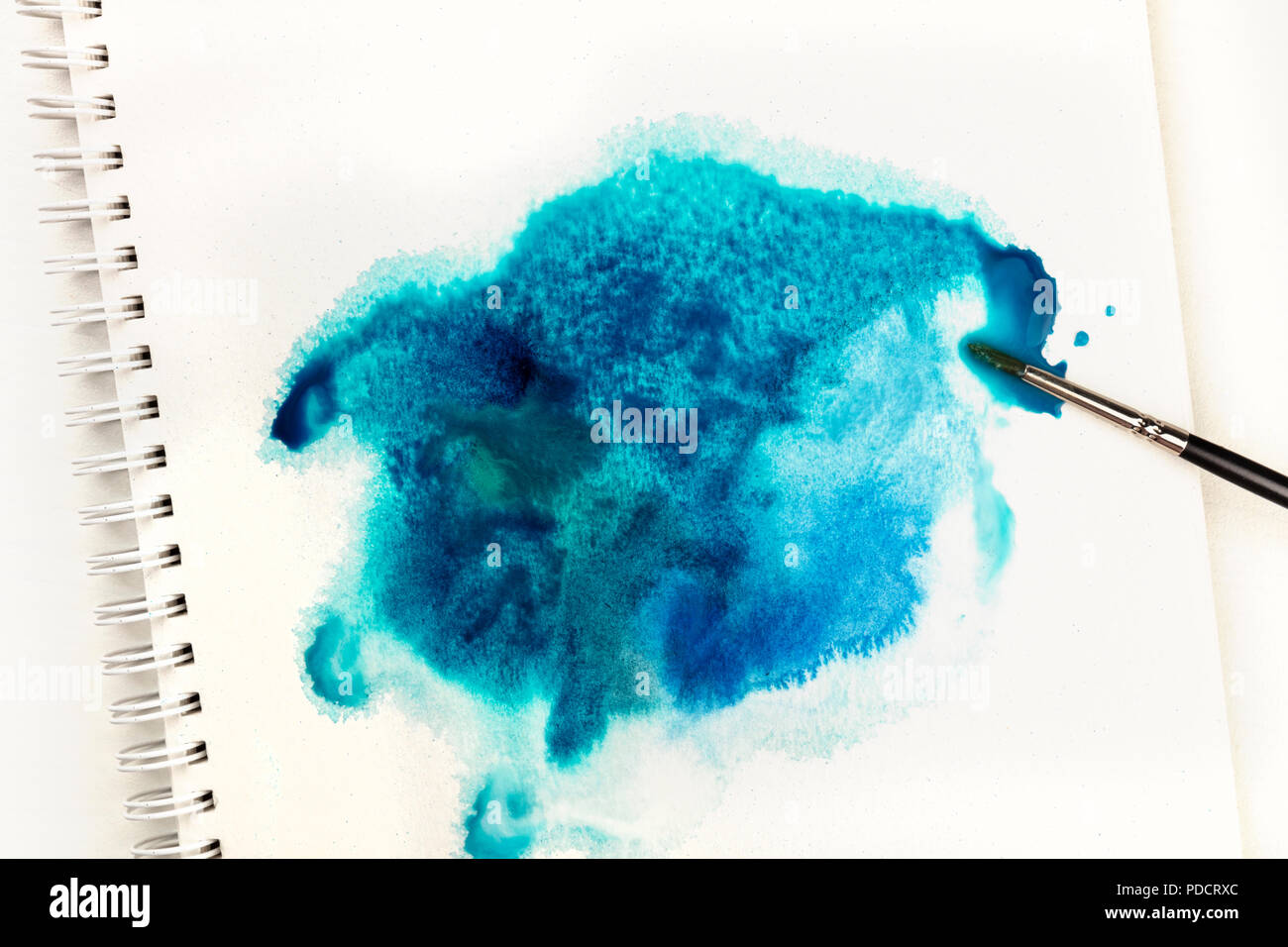 An overhead photo of a watercolor stain in a notebook with a brush and ...