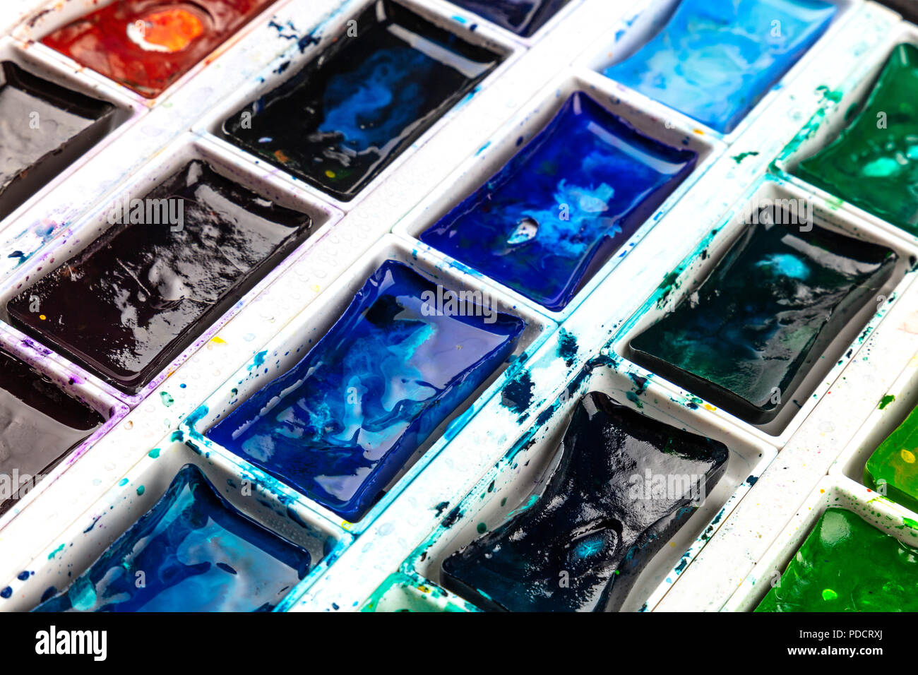A closeup photo of a vibrant watercolor box with wet paint, blue hues ...