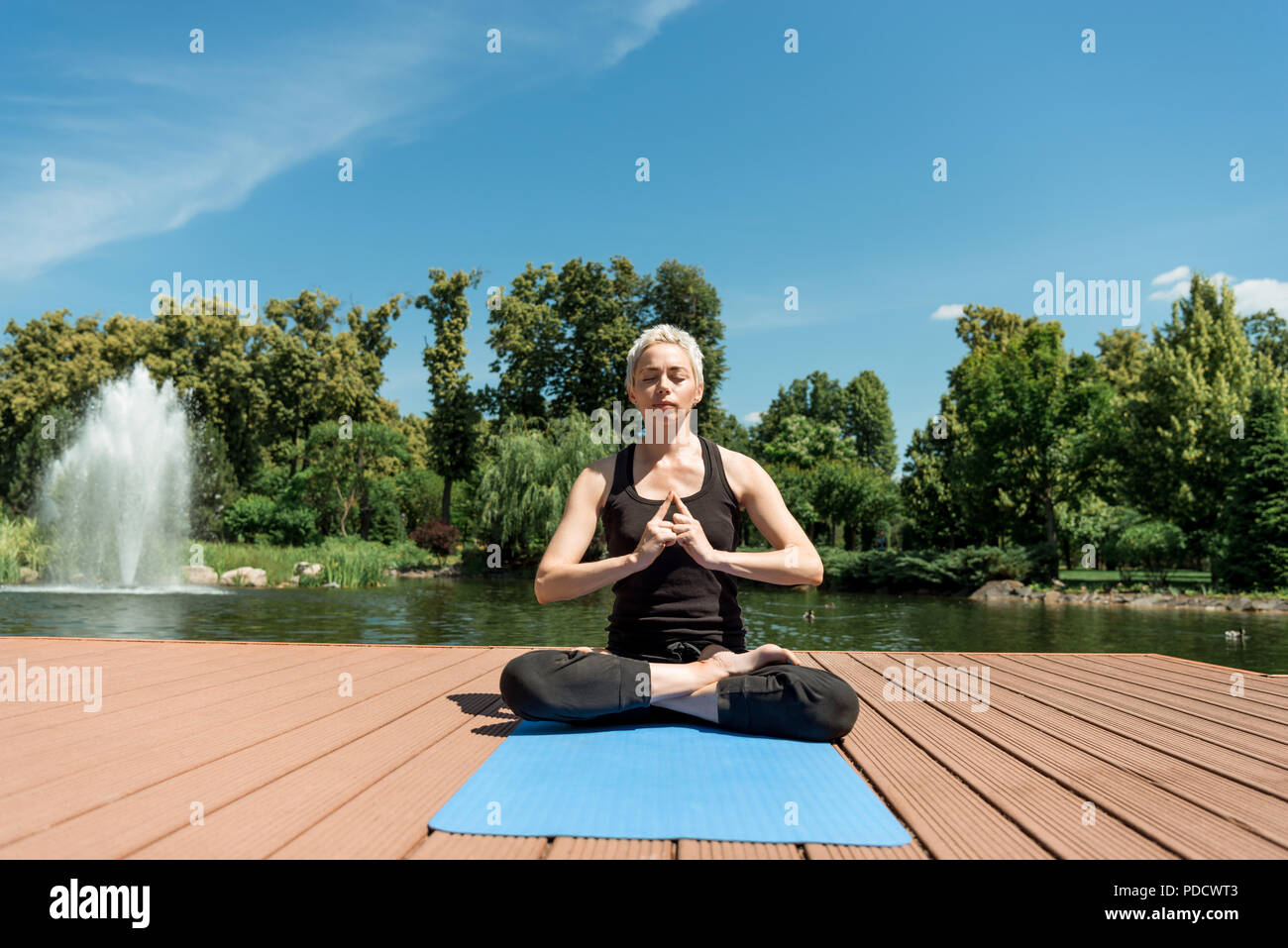 athletic woman practicing yoga in lotus pose on yoga mat near river in ...