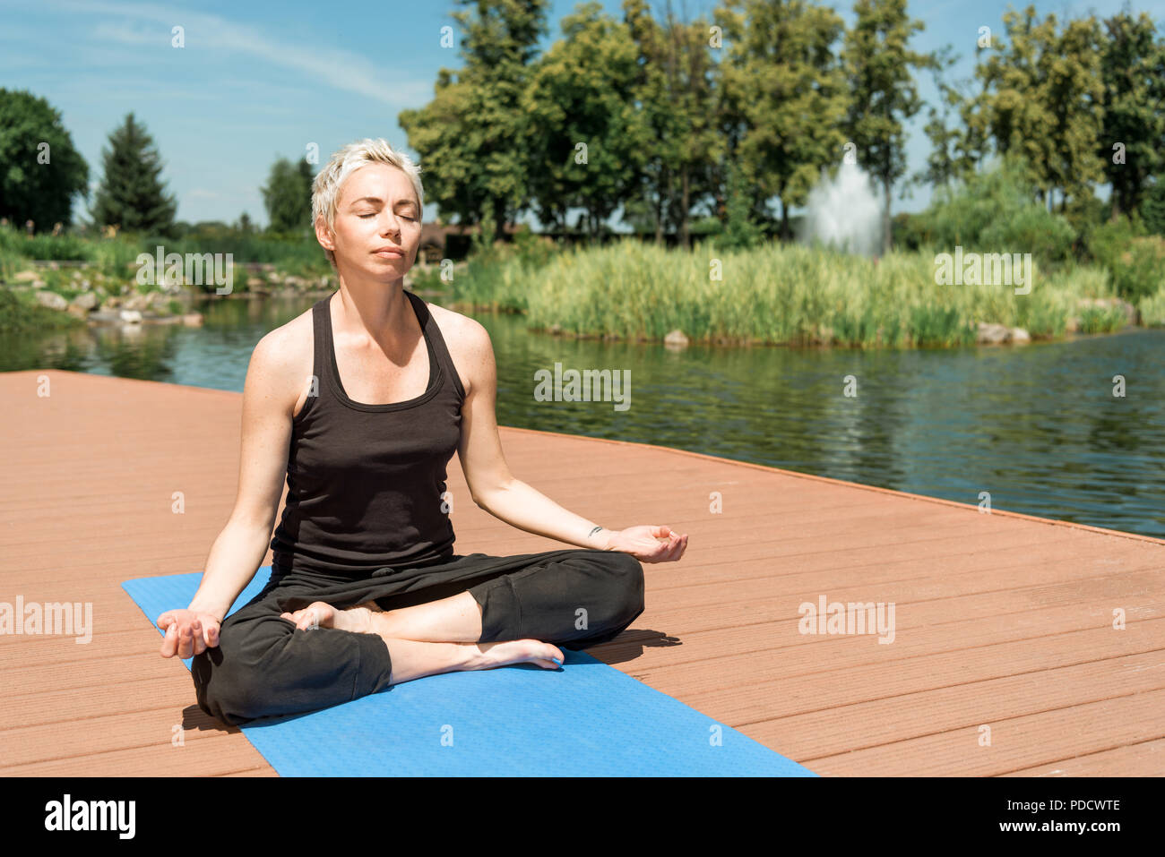 woman practicing yoga in lotus pose and meditating on yoga mat near ...