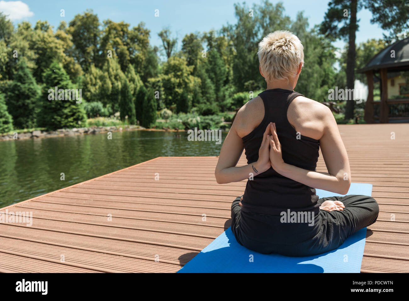 back view of woman practicing yoga in lotus pose and hands in namaste ...