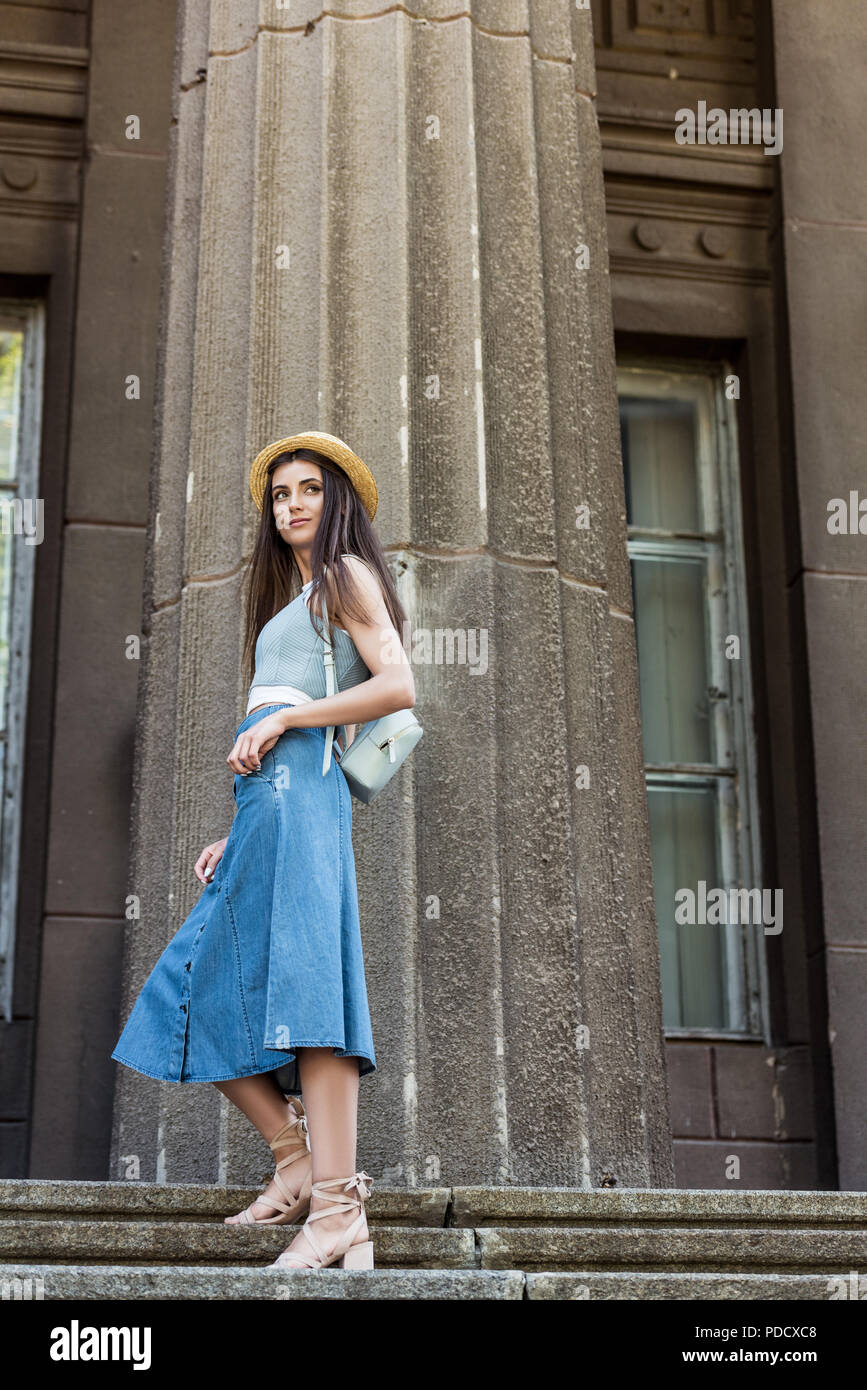 side view of young beautiful woman in straw hat standing on steps on ...