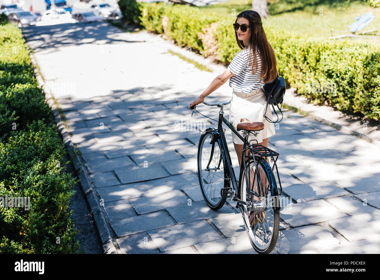 back view of young woman in sunglasses with retro bicycle on street ...