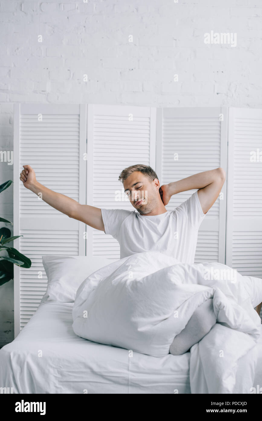 handsome young man sitting on bed and stretching at morning Stock Photo ...