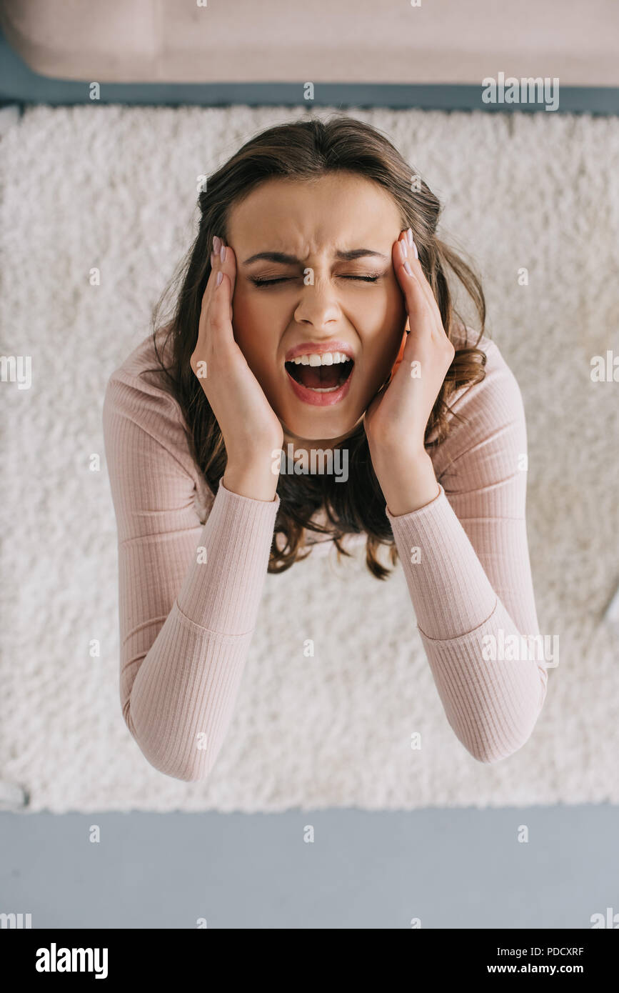 overhead view of young woman screaming and suffering from headache ...