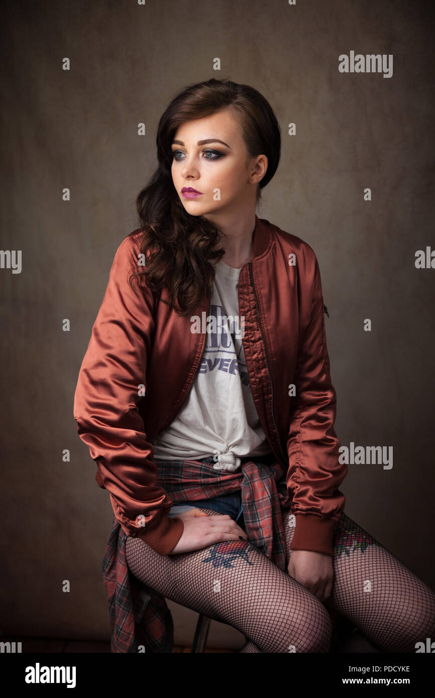 An alternative looking girl sitting down wearing a shiny bomber jacket ...