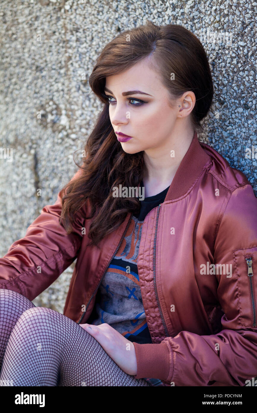 An alternative looking girl sitting down against a wall wearing a shiny ...
