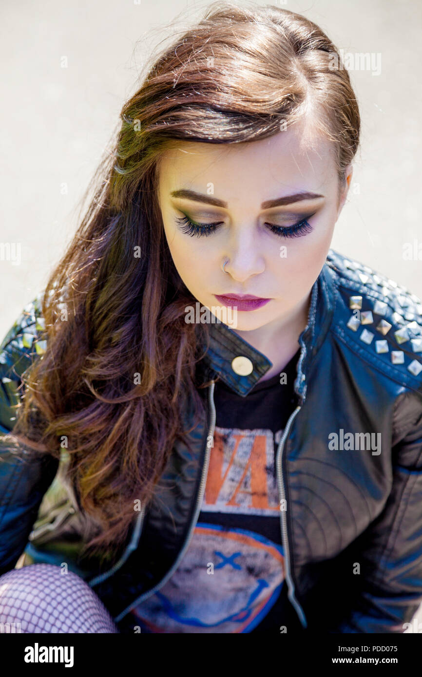 An alternative looking girl sitting down outside wearing a bikers ...