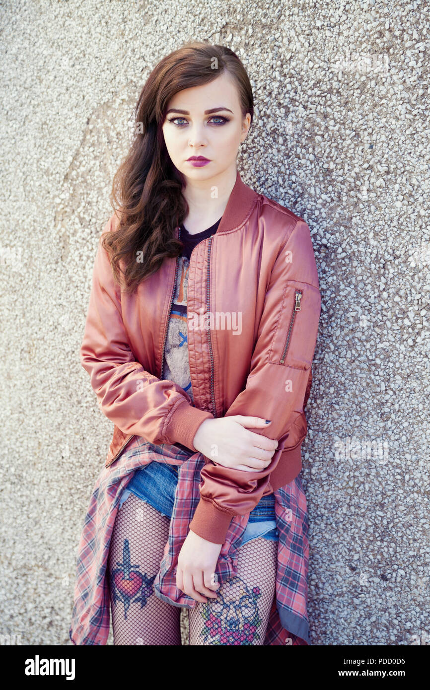 An alternative looking girl standing leaning against a wall wearing a ...