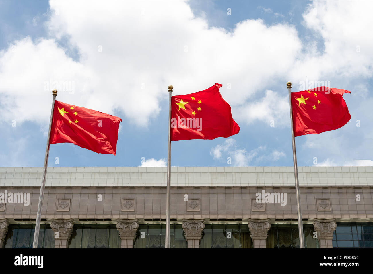 Three Chinese flags flying from poles with building in background Stock ...