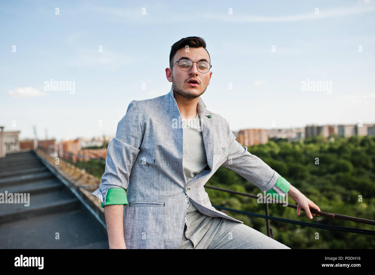 Dreamer stylish macho man in gray suit and glasses posed on the roof ...