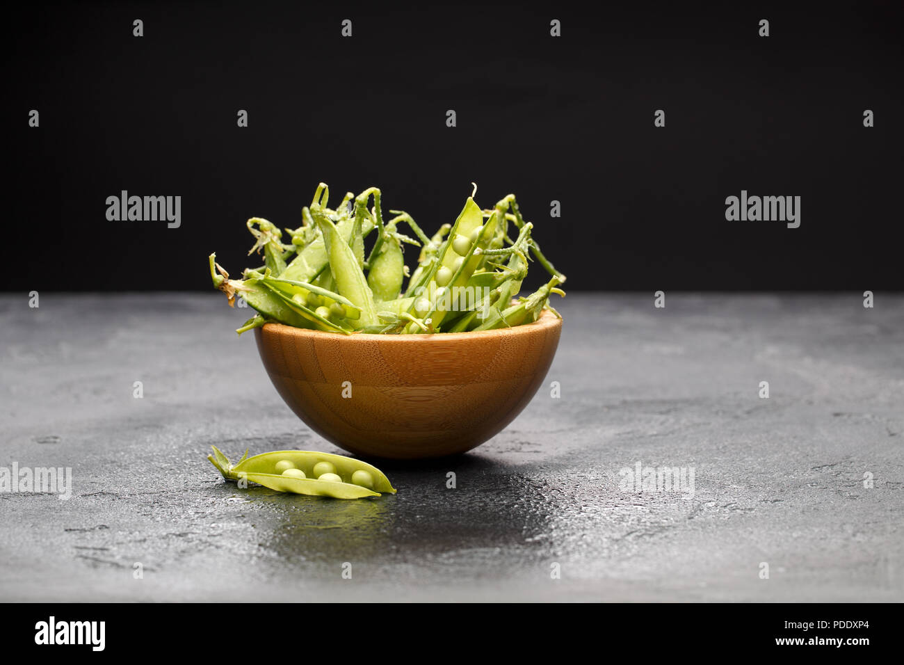 Photo of green pea pods in wooden plate on blank black table with pod ...