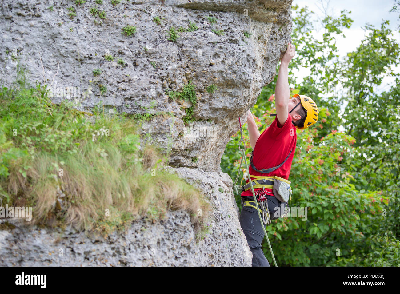 Photo of sports man in helmet clambering over rock against background ...