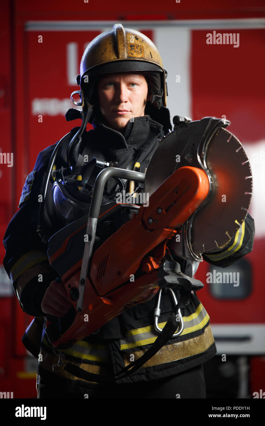 Photo of serious fireman wearing helmet with chainsaw on background of ...