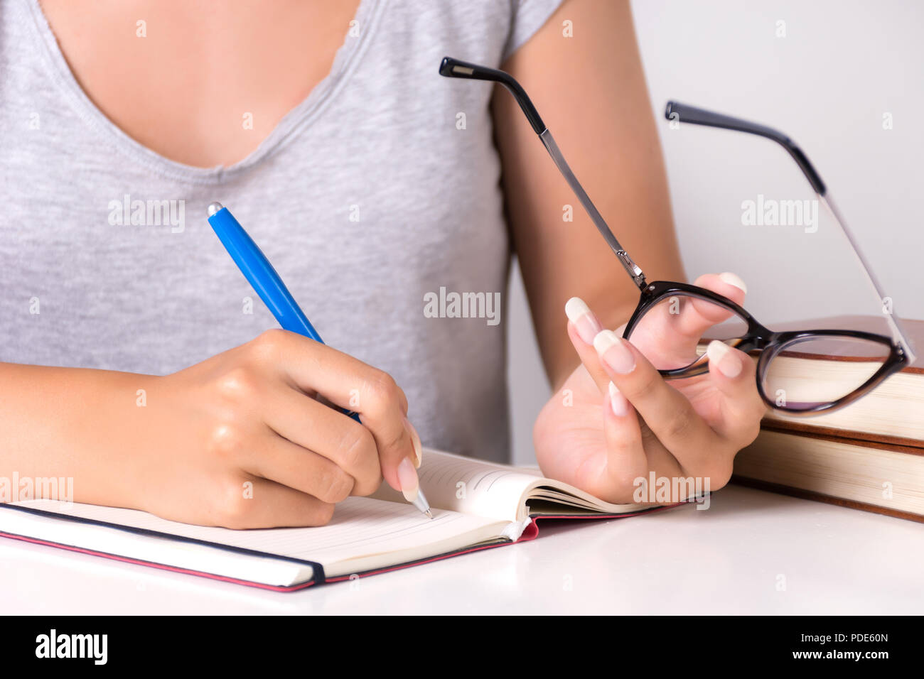 Beautiful girl student writes in notebook with pen and holding glasses ...