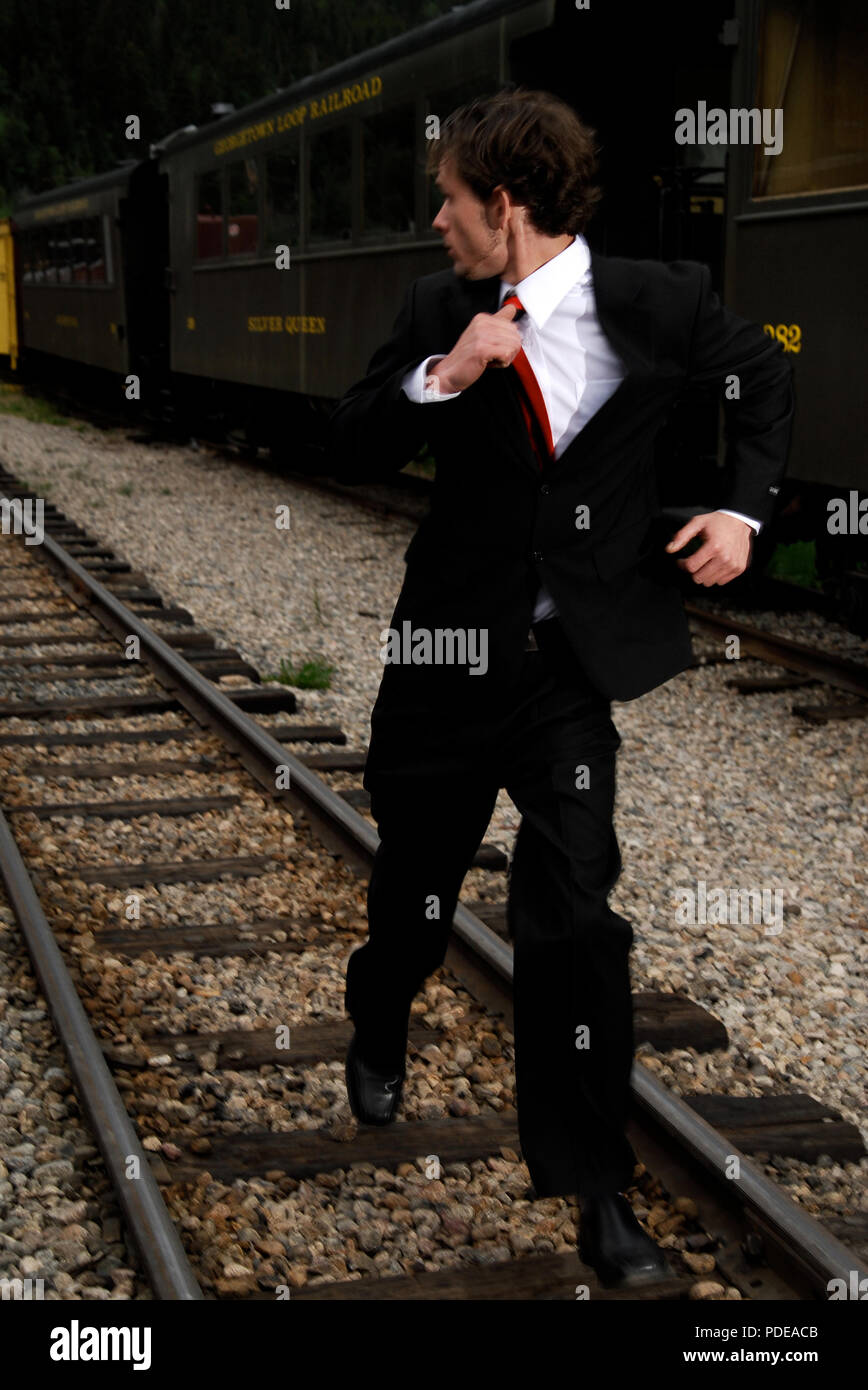 Young man in a suit running down narrow guage railroad tracks alongside ...