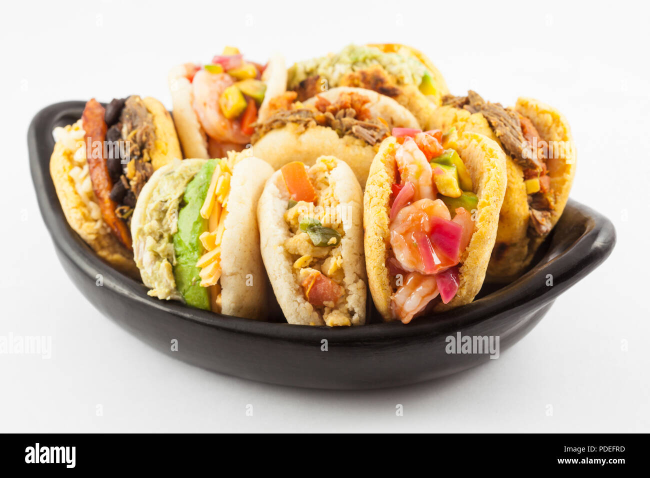 Arepas with assorted fillings served in a black ceramic dish on white ...