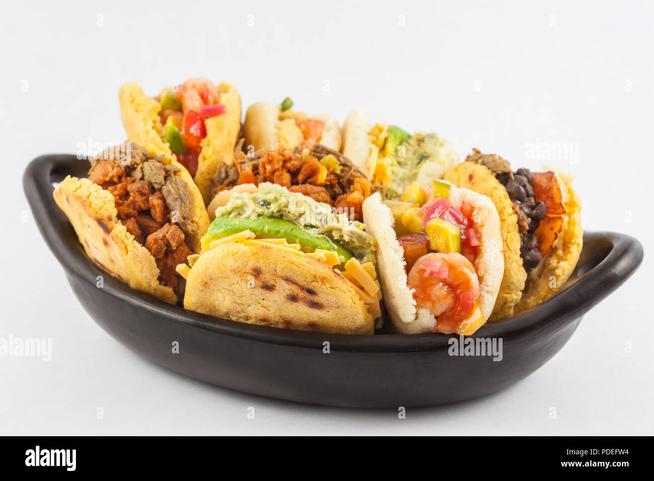 Arepas with assorted fillings served in a black ceramic dish on white ...