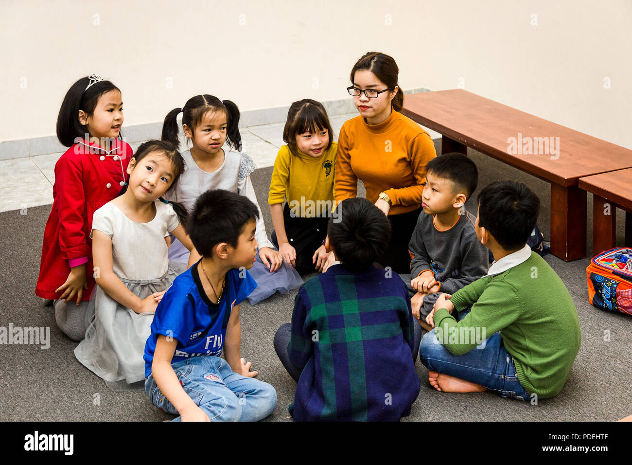 Small class of Asian students sitting in a circle with their teacher ...