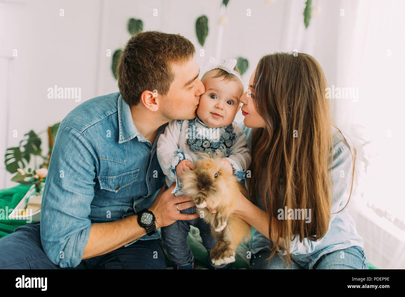 Family portrait. Parents are kissing the baby into the cheek and ...
