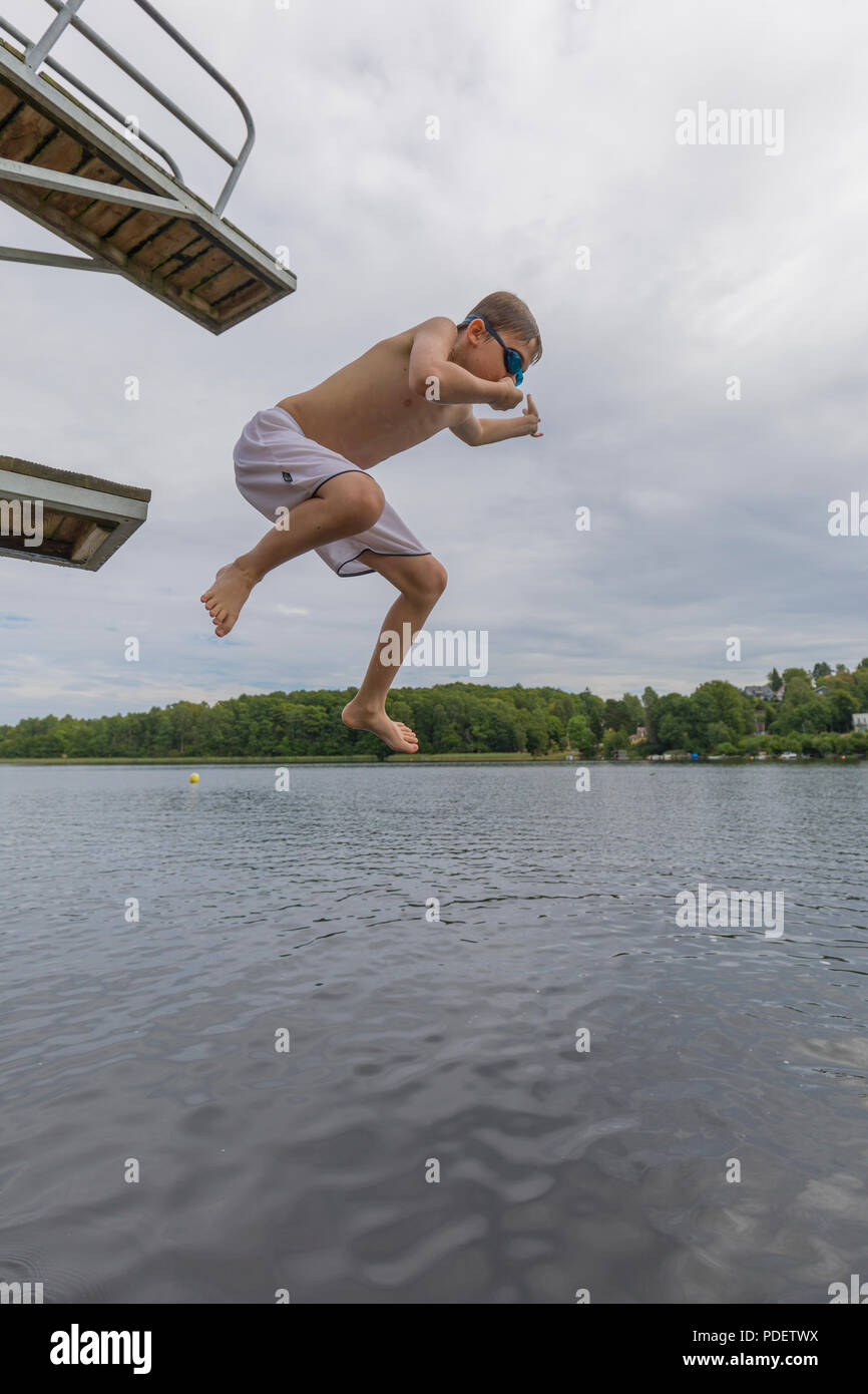 10 year old boy jumping into lake water from jetty jumping tower ...