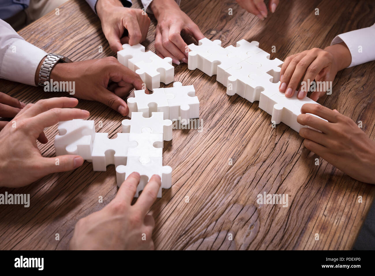Businesspeople Solving White Jigsaw Puzzle Together On Wooden Desk ...