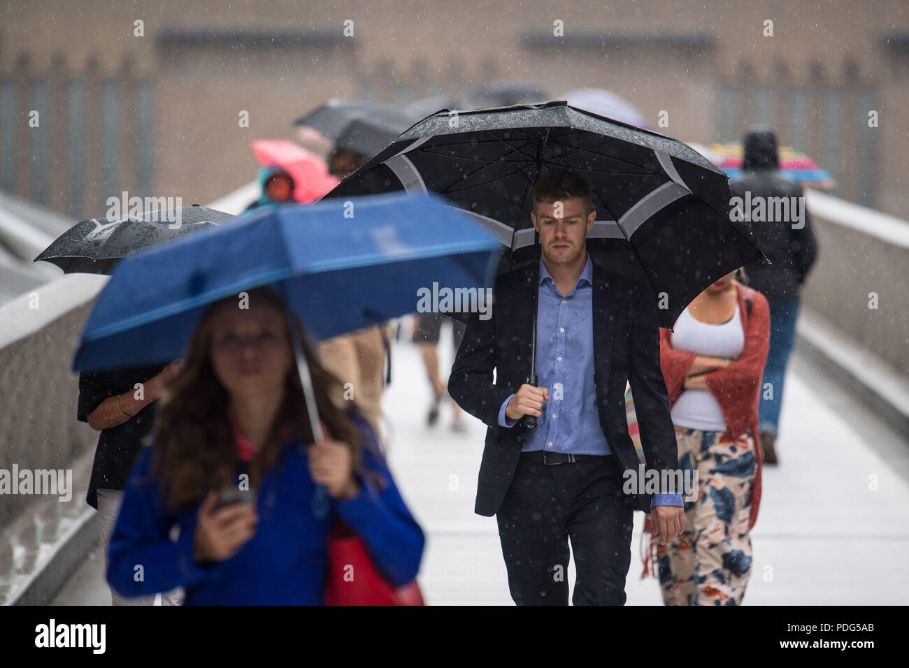 People shelter under umbrellas as they cross the Millennium Bridge ...