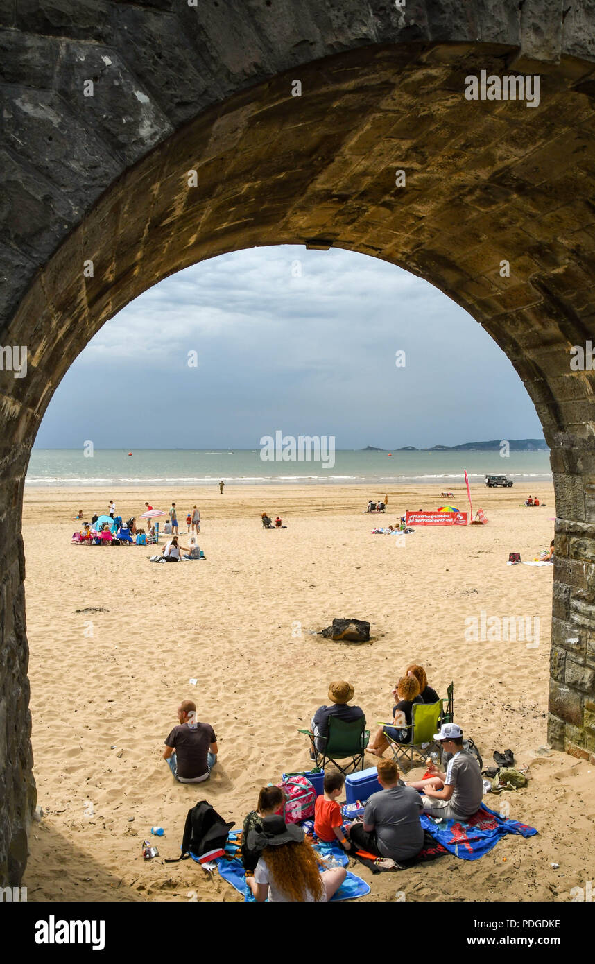 Family sheltering under an old stone arch on the beach in Swansea ...