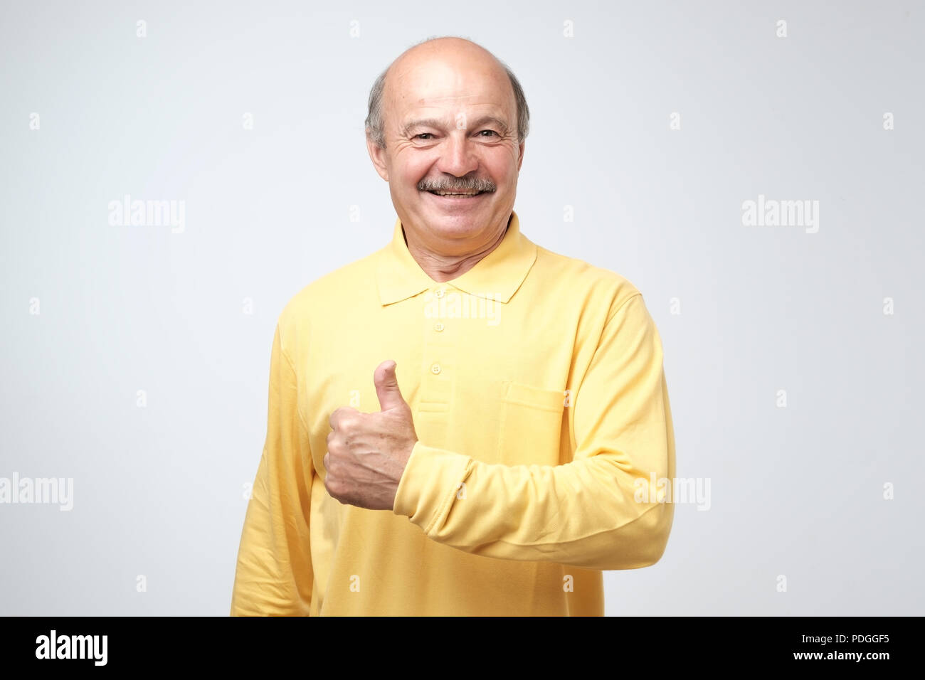 Handsome, bald man in yellow tshirt with his thumb up in sign of ...