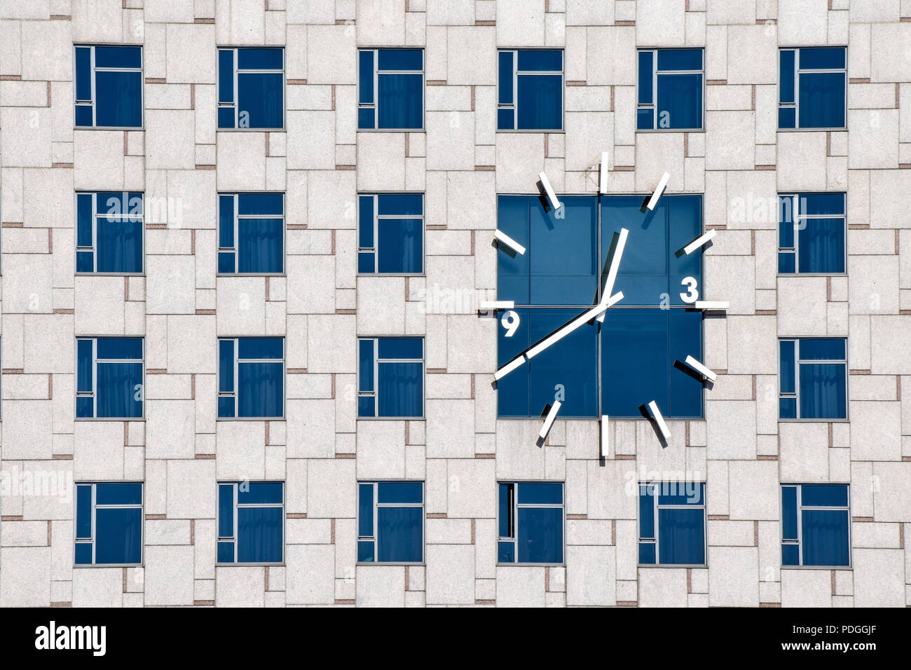 Clock on a contemporary building facade with multiple identical windows ...
