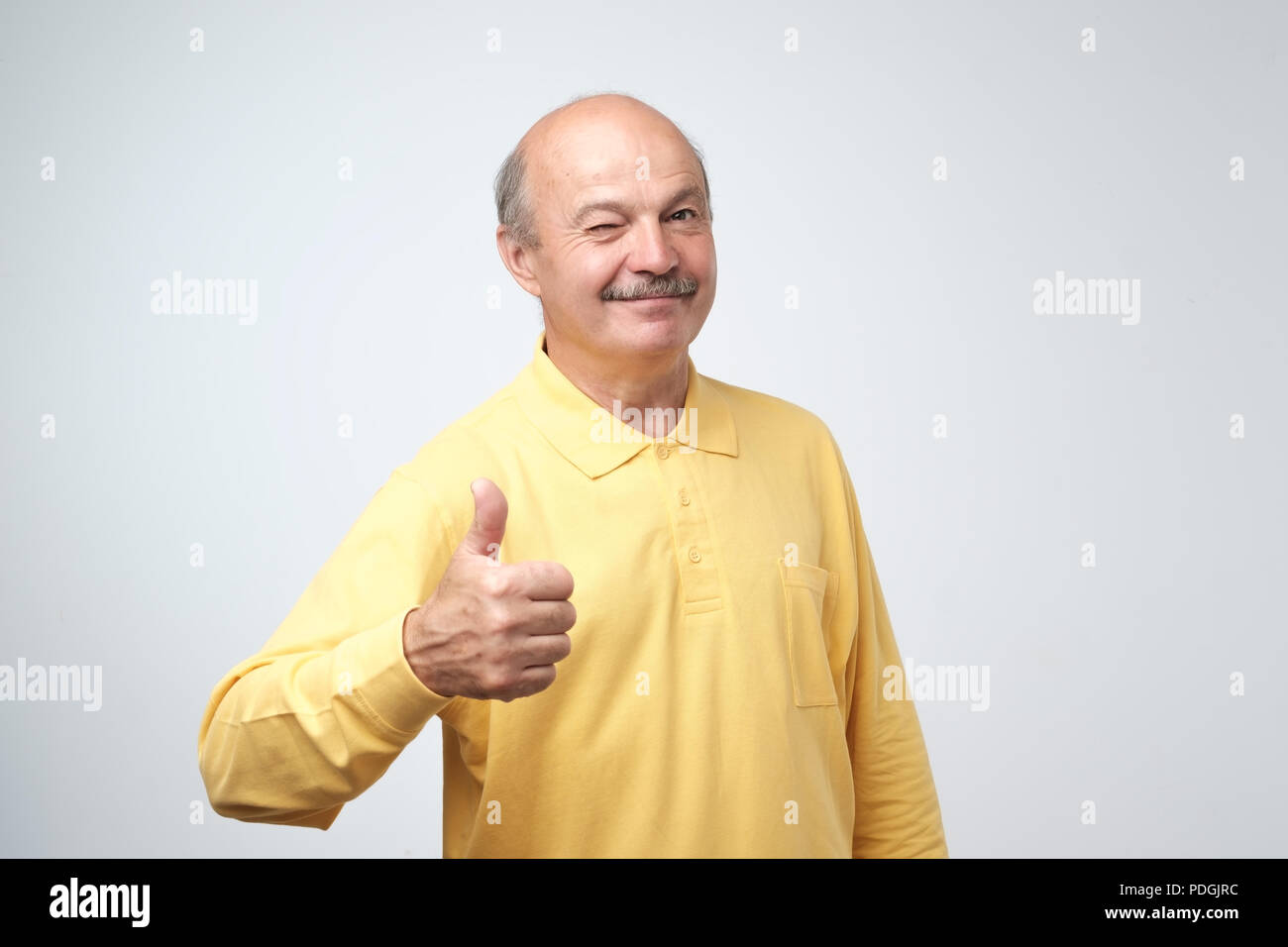 Handsome, bald man in yellow tshirt with his thumb up in sign of ...