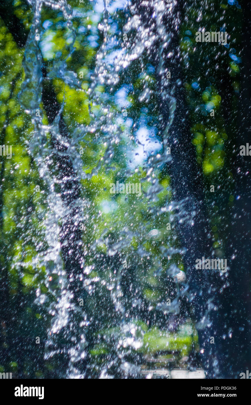 transparent falling water vertical flows against a blue sky and green ...
