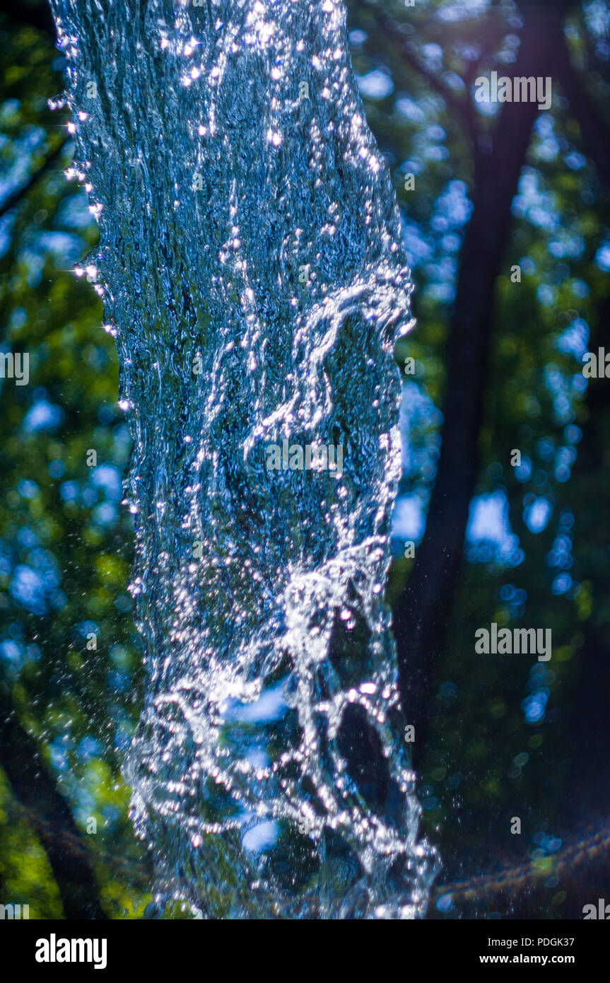 transparent falling water vertical flows against a blue sky and green ...