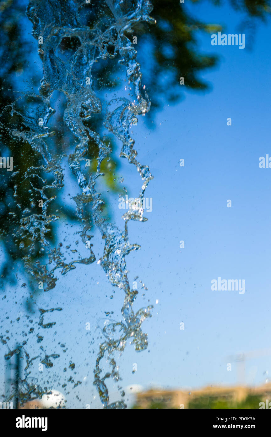 transparent falling water vertical flows against a blue sky and green ...