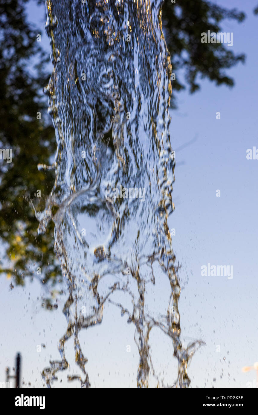 transparent falling water vertical flows against a blue sky and green ...