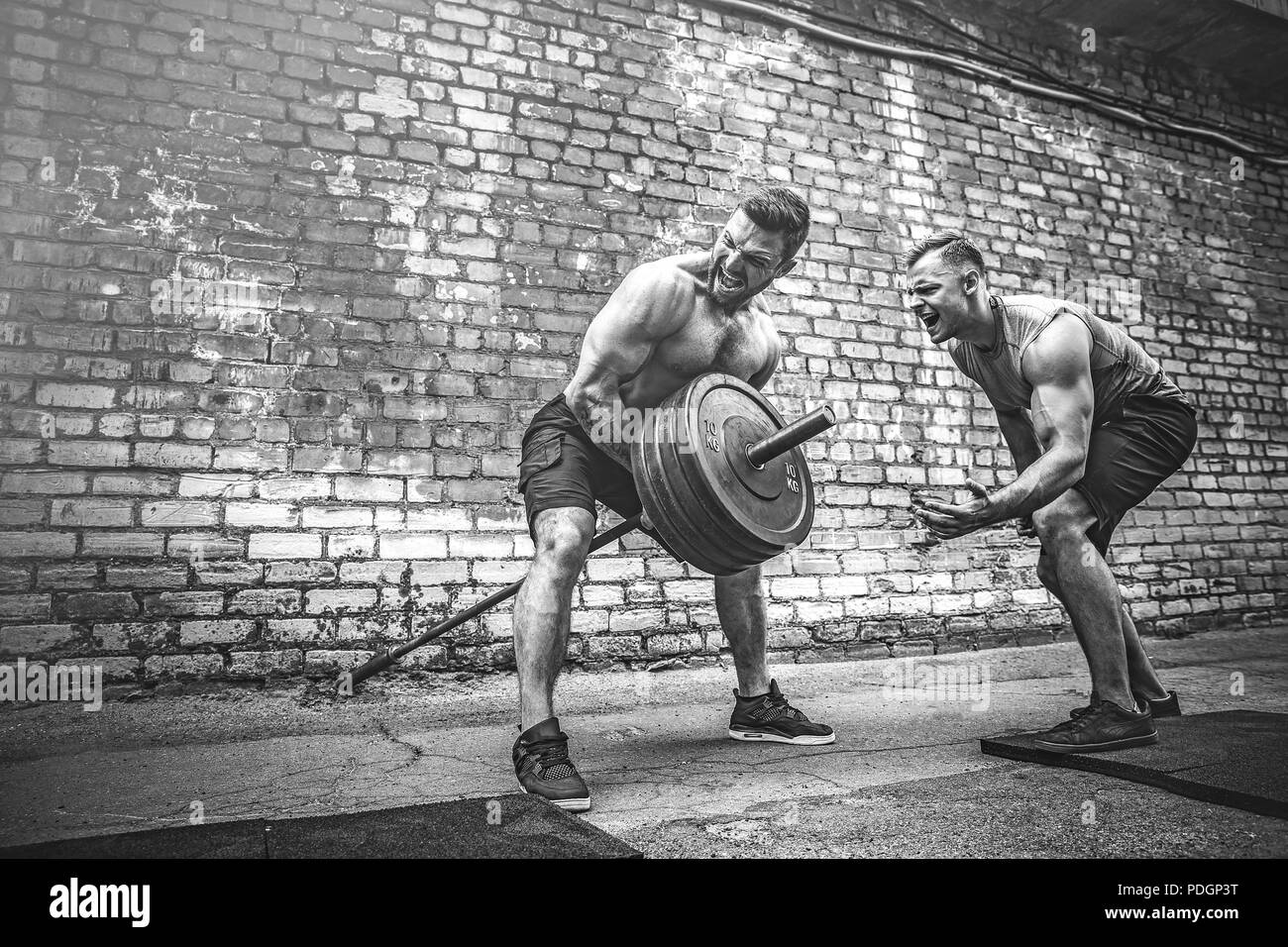 Two muscular athletes training, one raise the bar when other is ...